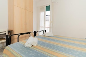 Quarto com cama, guarda-roupa de madeira, escrivaninha e janela com cortinas.