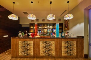 Uma área de bar com painéis de madeira, luminárias de vidro colorido penduradas e diversos objetos decorativos no balcão.