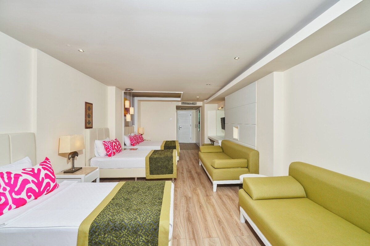 Quarto de hotel com uma cama, duas mesas de cabeceira, um sofá, uma poltrona e uma pequena mesa.