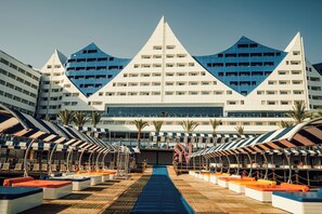 Um hotel com arquitetura triangular marcante, área de piscina com espreguiçadeiras e céu claro.