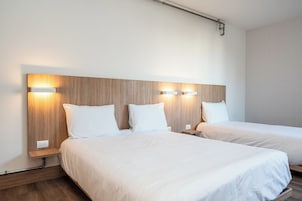 Quarto de hotel com duas camas, cabeceiras de madeira e iluminação fixa na parede.