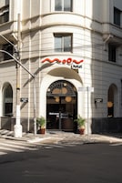 Entrada de hotel com fachada curva, uma grande porta em arco e um letreiro sobre a entrada.