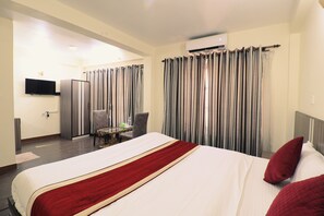 Quarto de hotel com cama, televisão, cadeira e cortinas.