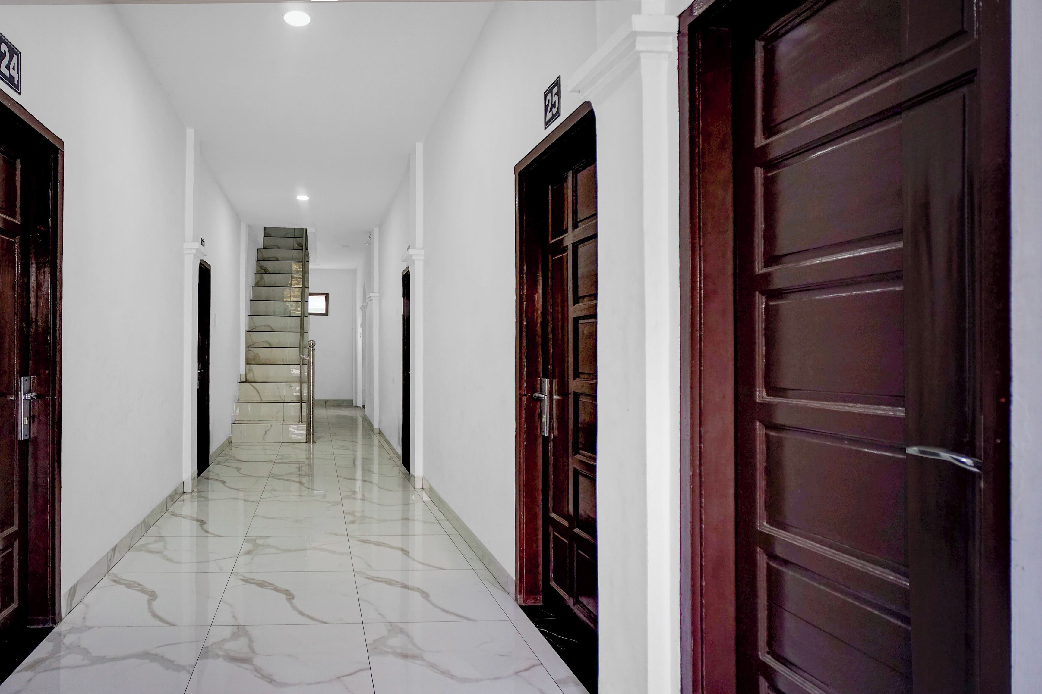 Um corredor com piso de mármore, portas de madeira e escada que leva a um andar superior.