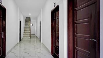 Um corredor com piso de mármore, portas de madeira e escada que leva a um andar superior.