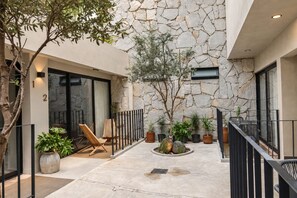 Um pátio moderno ao ar livre com paredes de pedra, área de estar com cadeiras e vasos de plantas.