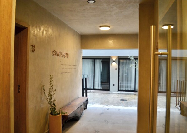 Um corredor com um banco de madeira, uma parede com uma placa e uma porta com o número 3.