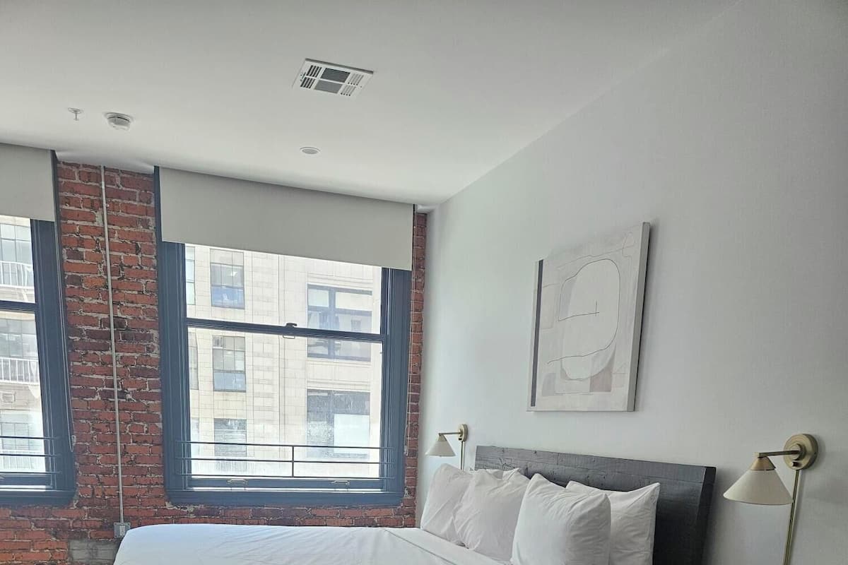 Quarto moderno com cama grande, parede de tijolos e janela.