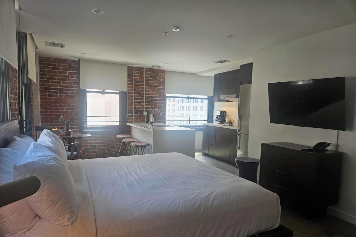 Quarto de hotel moderno com cama grande, televisão, área de cozinha e vista para a cidade.