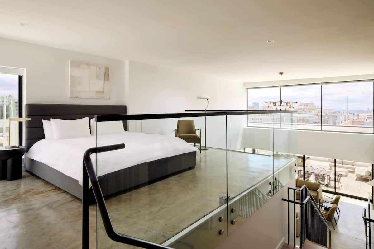 Quarto de hotel moderno com uma cama grande, varanda de vidro e vista para a cidade.