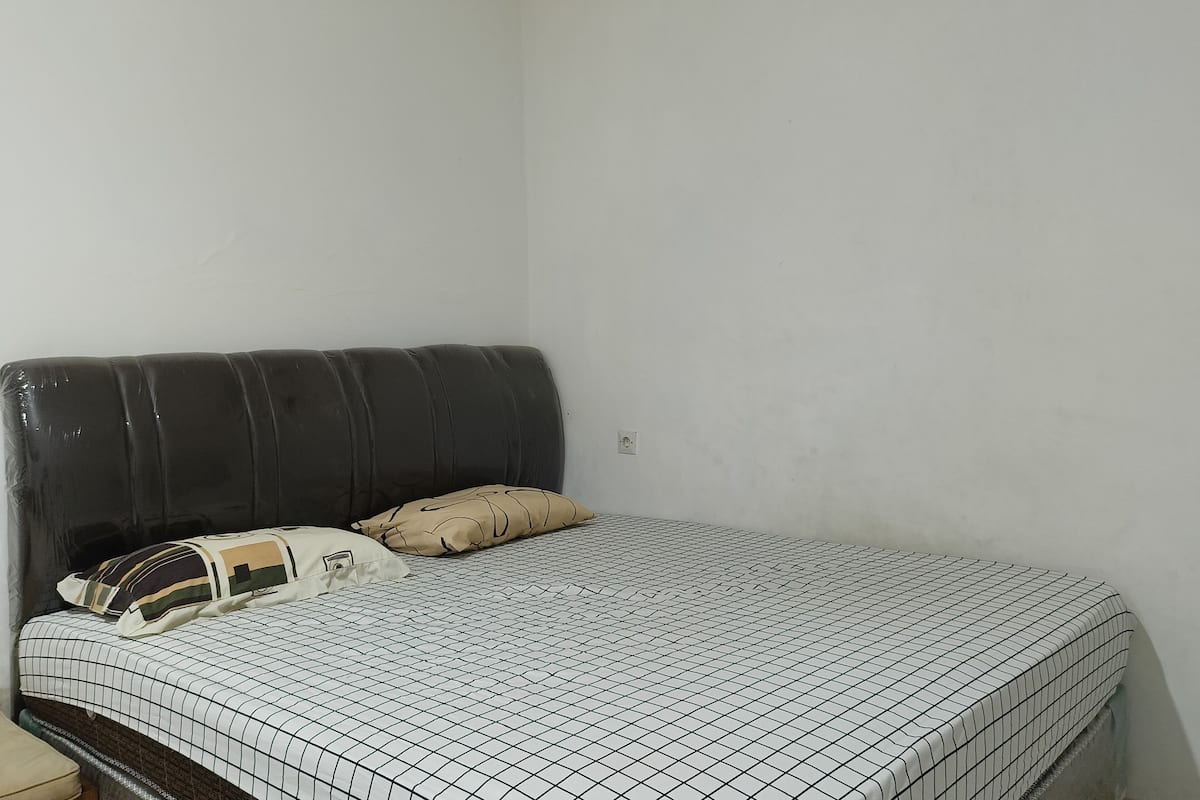 Uma cama de solteiro com cabeceira preta, colcha estampada e dois travesseiros.