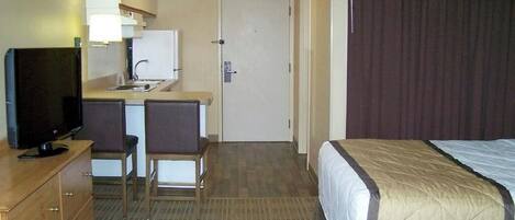 Quarto de hotel com cama, mesa de trabalho com cadeira, televisão e porta.