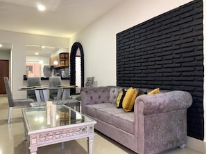 Uma sala de estar moderna com uma mesa de centro de vidro, um sofá macio e uma parede com padrão de tijolos pretos.