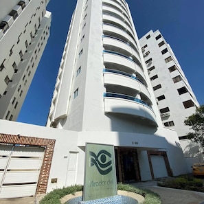 Um edifício moderno de vários andares com fachada curva, uma placa com a inscrição 'Mirador del Litoral' e uma área de estacionamento com um carro amarelo.