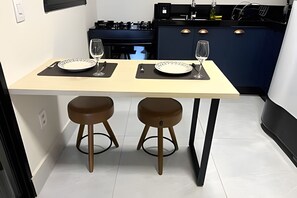 Cozinha com mesa de jantar para dois, dois banquinhos e fogão a gás.