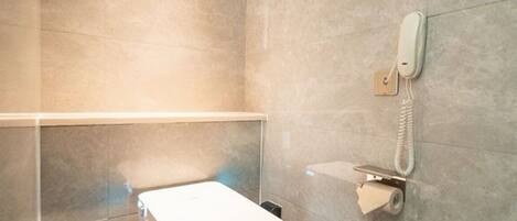 Um banheiro moderno com vaso sanitário, lixeira e telefone fixado na parede.