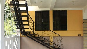 Uma escadaria com grades de metal ornamentadas, uma parede amarela e uma janela com barras pretas.