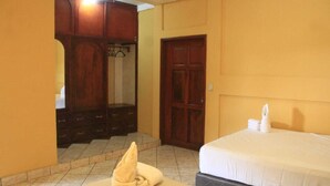 Quarto de hotel com cama, guarda-roupa de madeira, espelho e chão em mosaico.