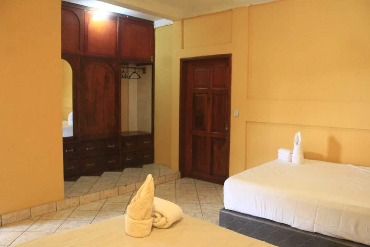 Quarto de hotel com cama, guarda-roupa de madeira, espelho e chão em mosaico.