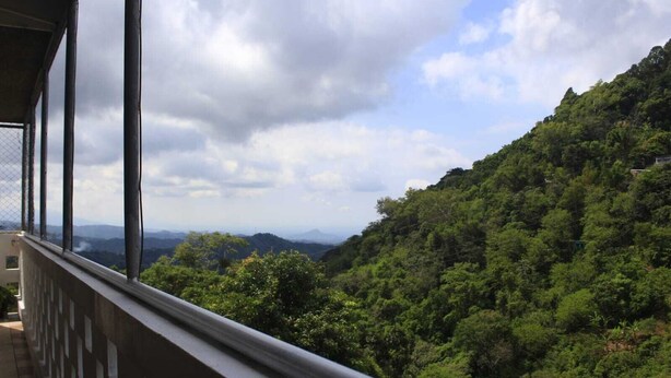 Varanda com vista para um morro verdejante e montanhas distantes.