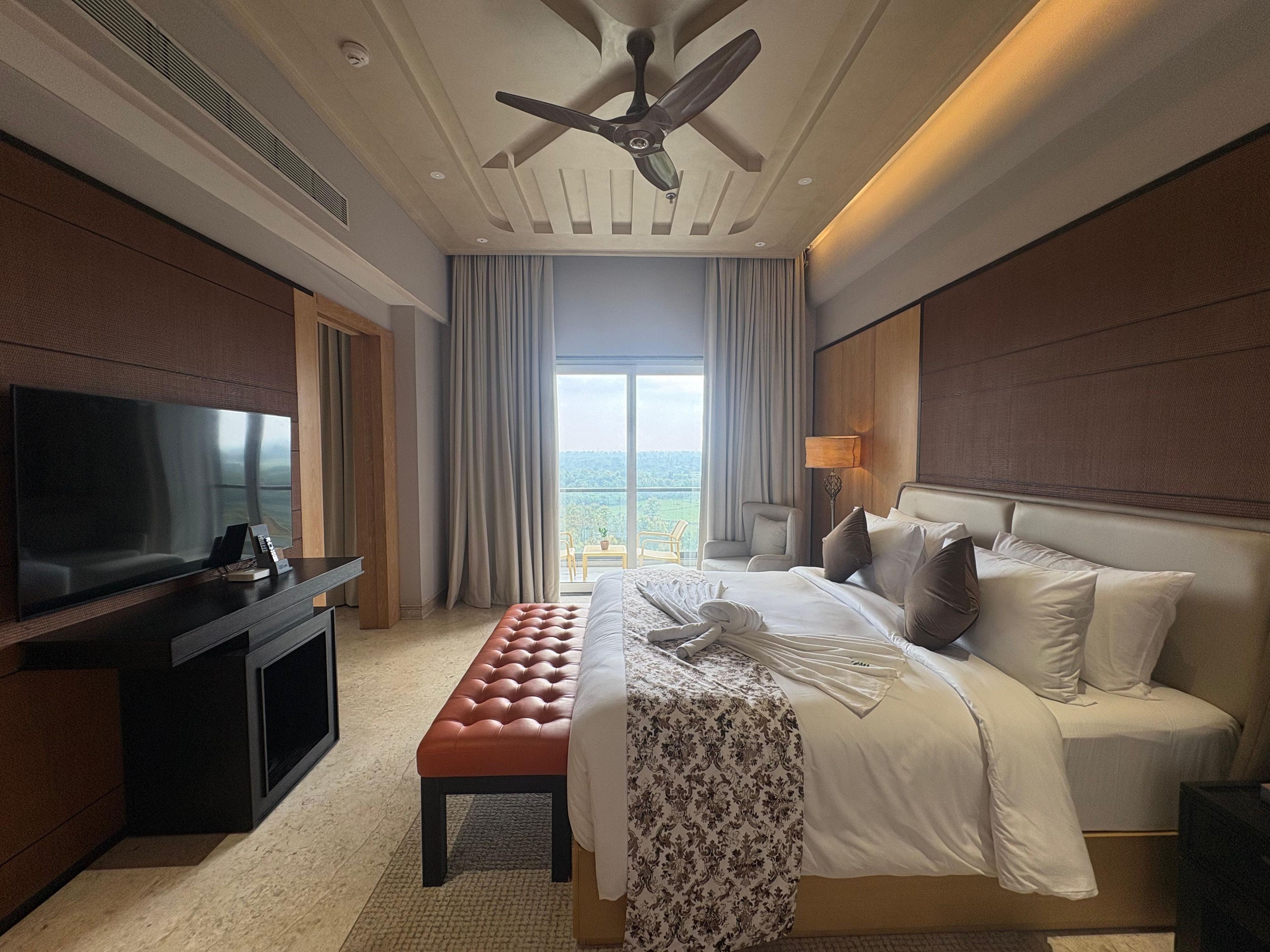 Quarto de hotel com televisão de tela plana, cama com dossel, ventilador de teto e vista para o exterior.