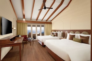 Quarto de hotel com duas camas, televisão, escrivaninha e vista para o oceano.