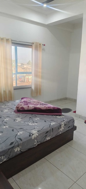 Quarto com cama, janela com cortinas, vista de edifícios e chão de azulejos.