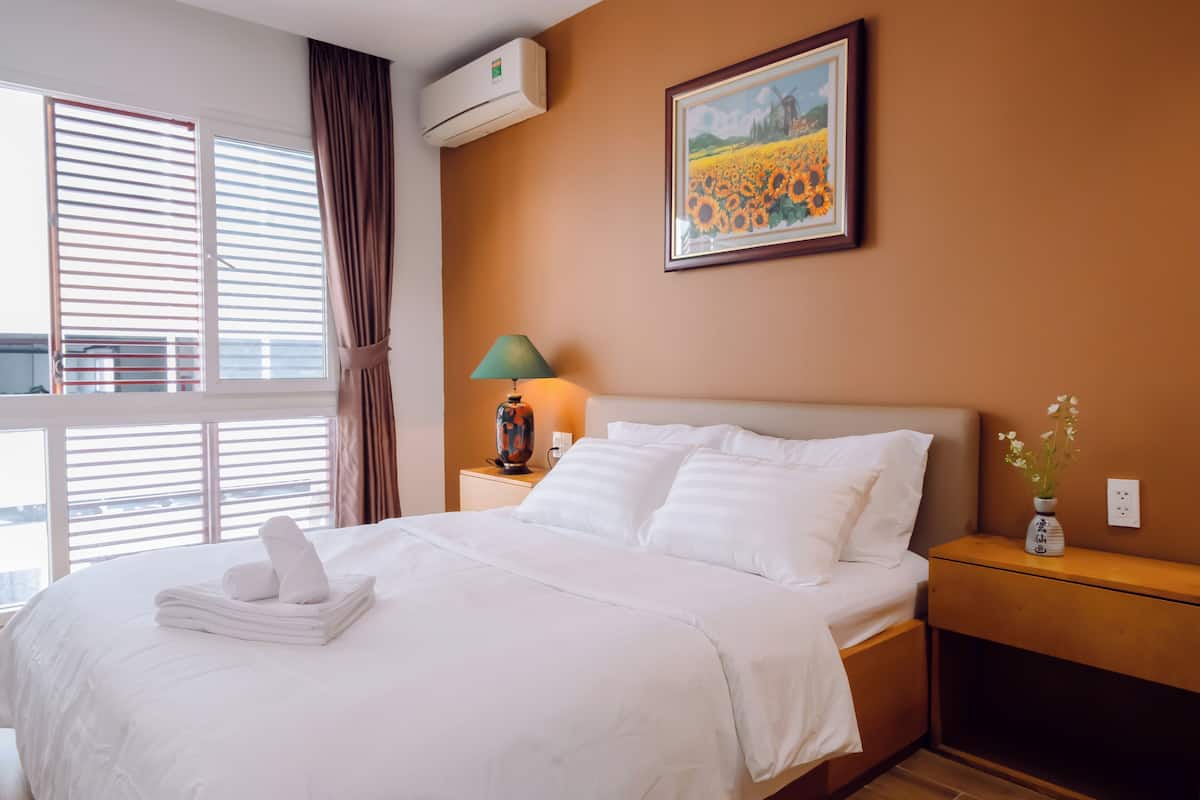 Quarto de hotel com cama, mesa de cabeceira com luminária, um quadro na parede e um ar condicionado.
