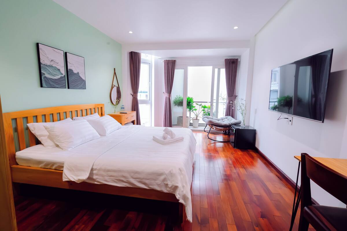 Quarto de hotel moderno com cama de madeira, televisão de tela plana e varanda com cortinas.