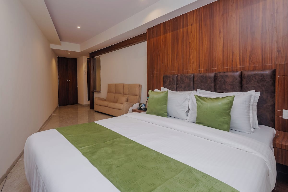 Quarto de hotel com uma cama grande, um sofá, painéis de madeira nas paredes e uma porta que dá para outro cômodo.