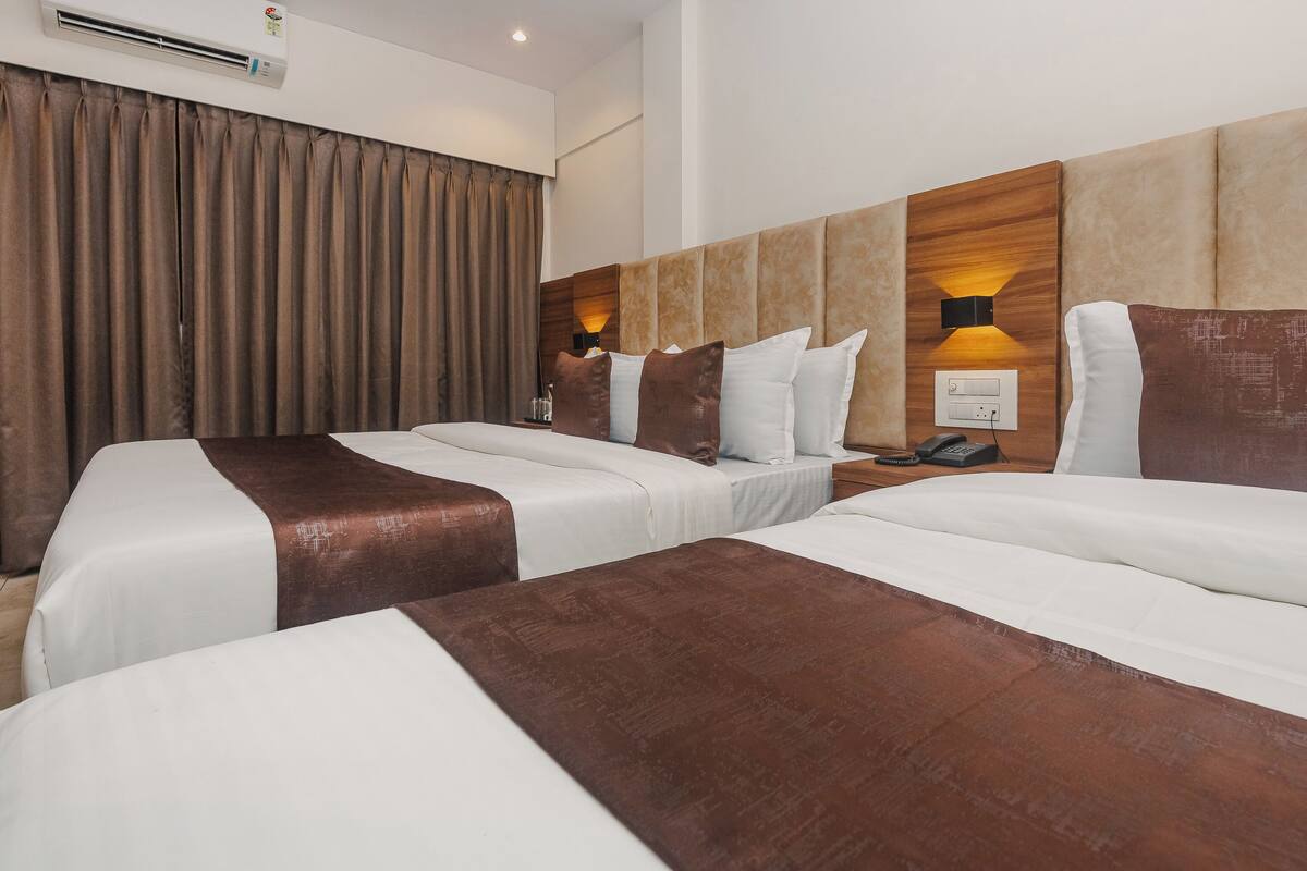 Quarto de hotel com duas camas, uma janela grande com cortinas, telefone fixado na parede e luminária na parede.