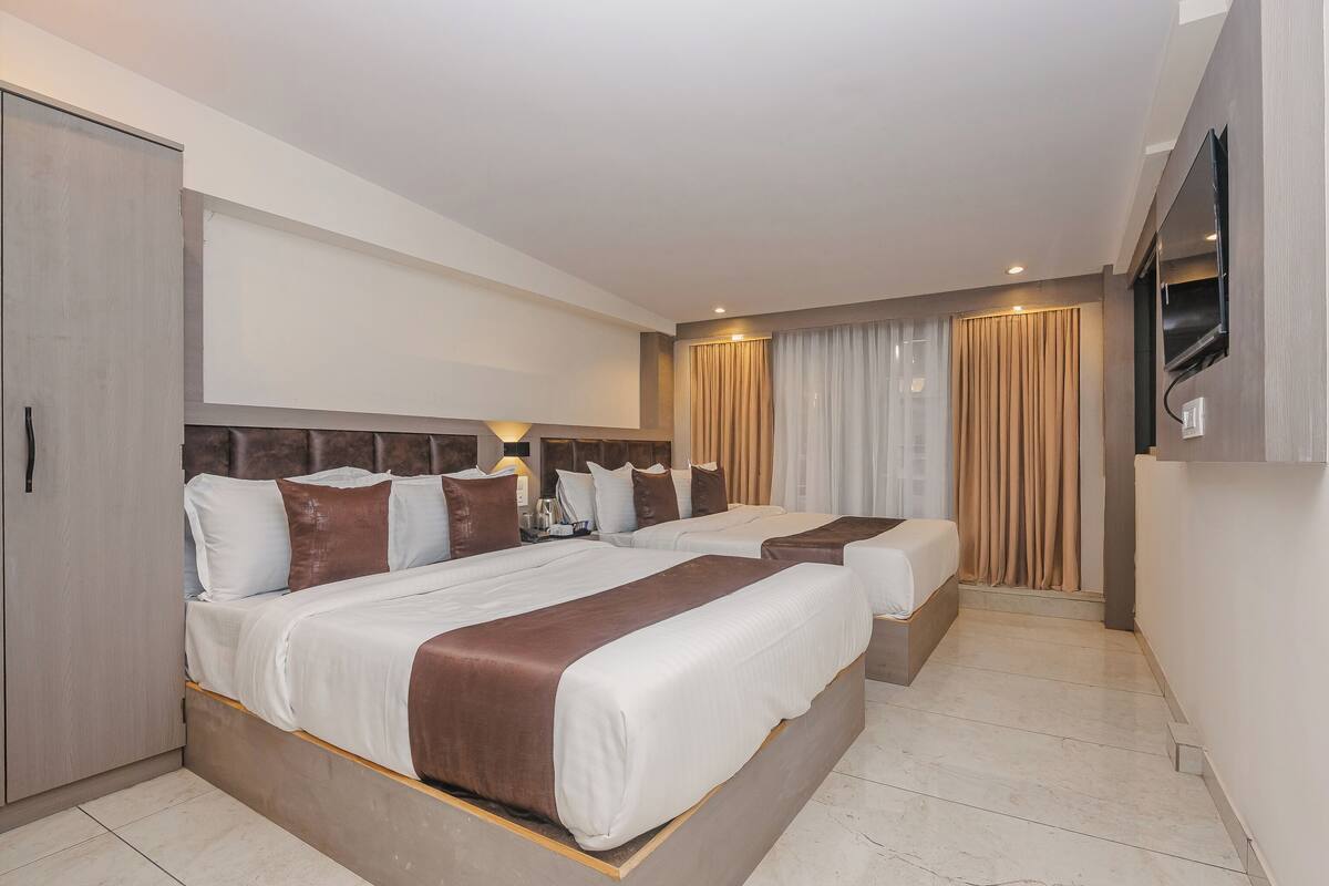 Quarto de hotel com duas camas, televisão, guarda-roupa e cortina.
