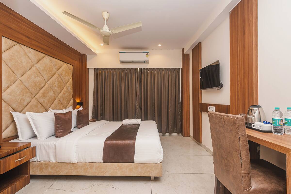 Quarto de hotel com cama, escrivaninha, cadeira, televisão e ar condicionado.