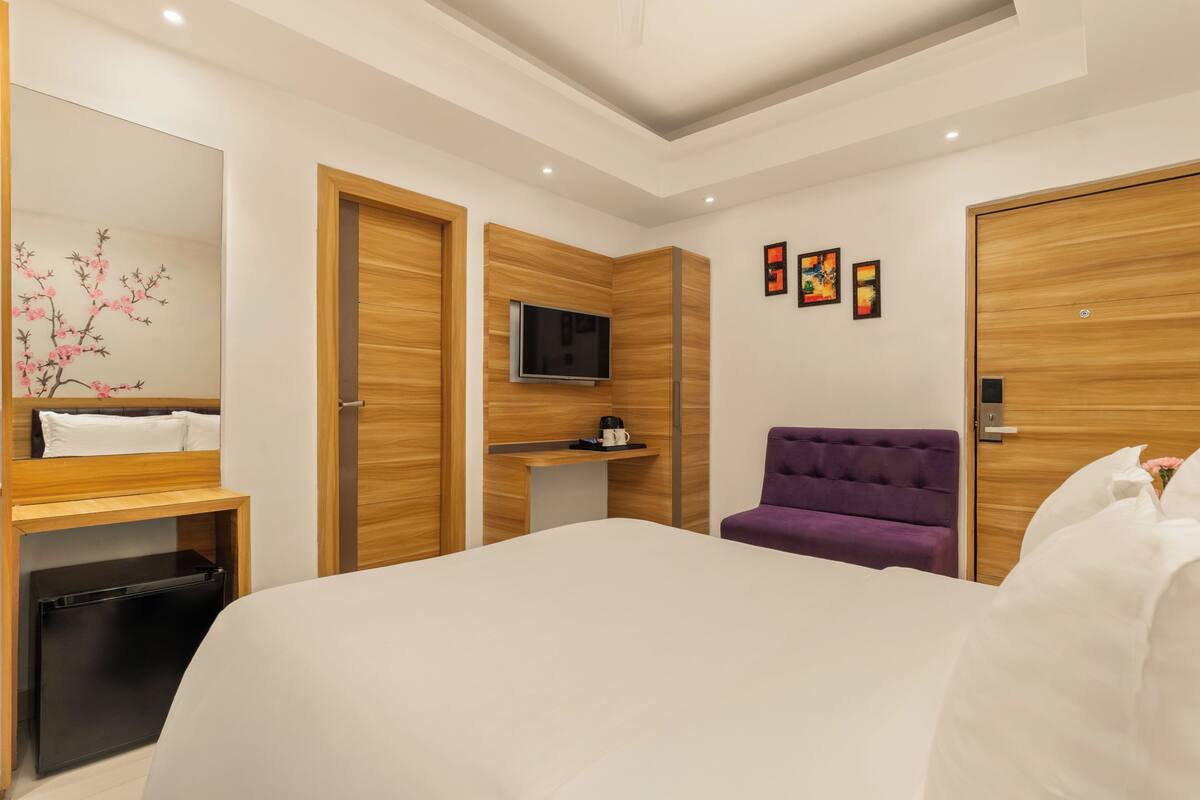 Quarto de hotel moderno com cama, televisão, pequena mesa, cadeira roxa e paredes de madeira.