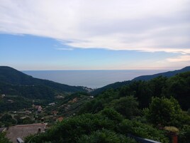 Paisagem costeira com colinas, céu claro e vista distante do mar.