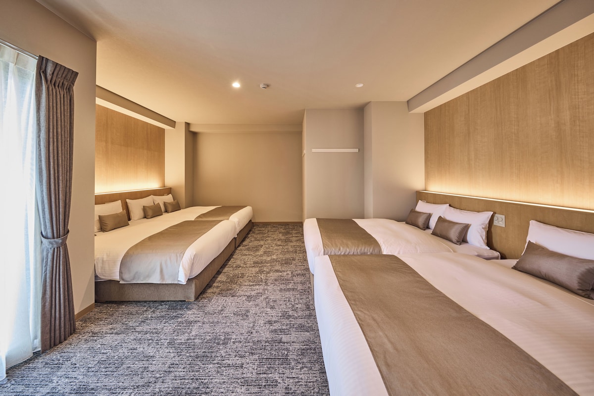 Quarto de hotel com duas camas, piso coberto por carpete e uma janela grande com cortinas.