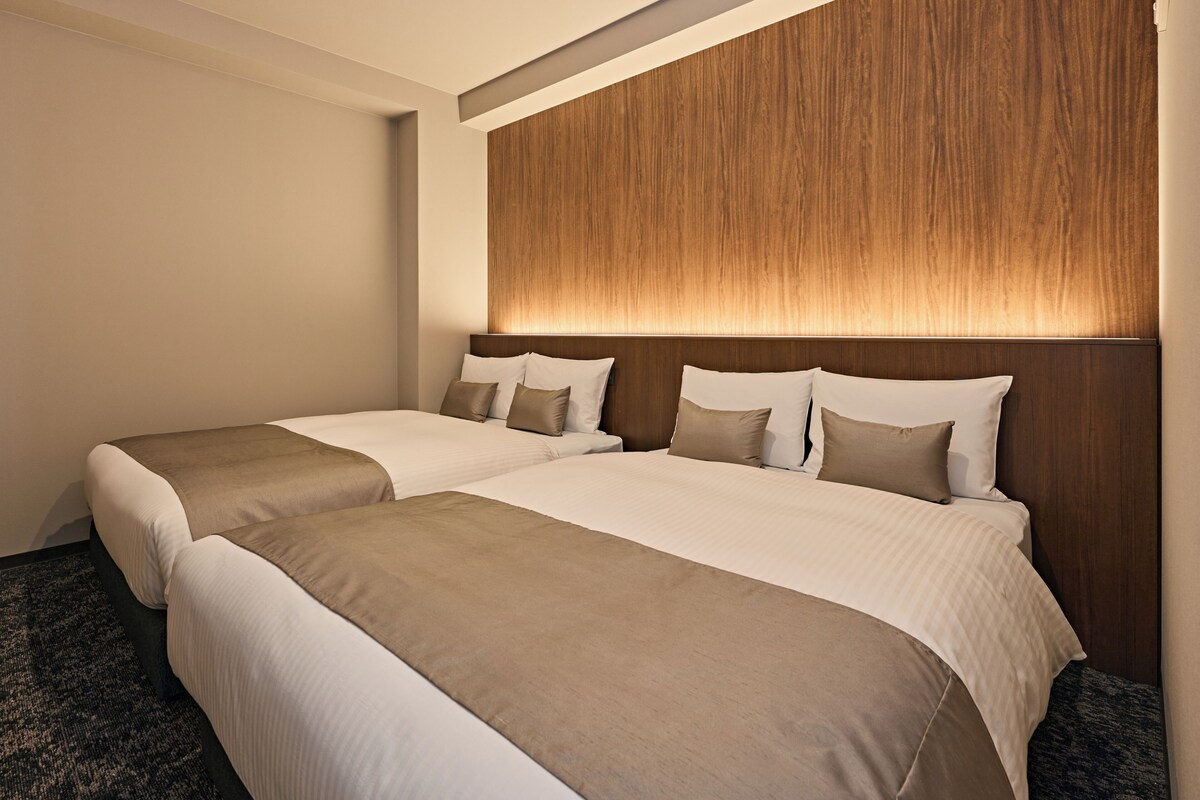 Quarto de hotel com duas camas, cabeceira de madeira e piso coberto por carpete.