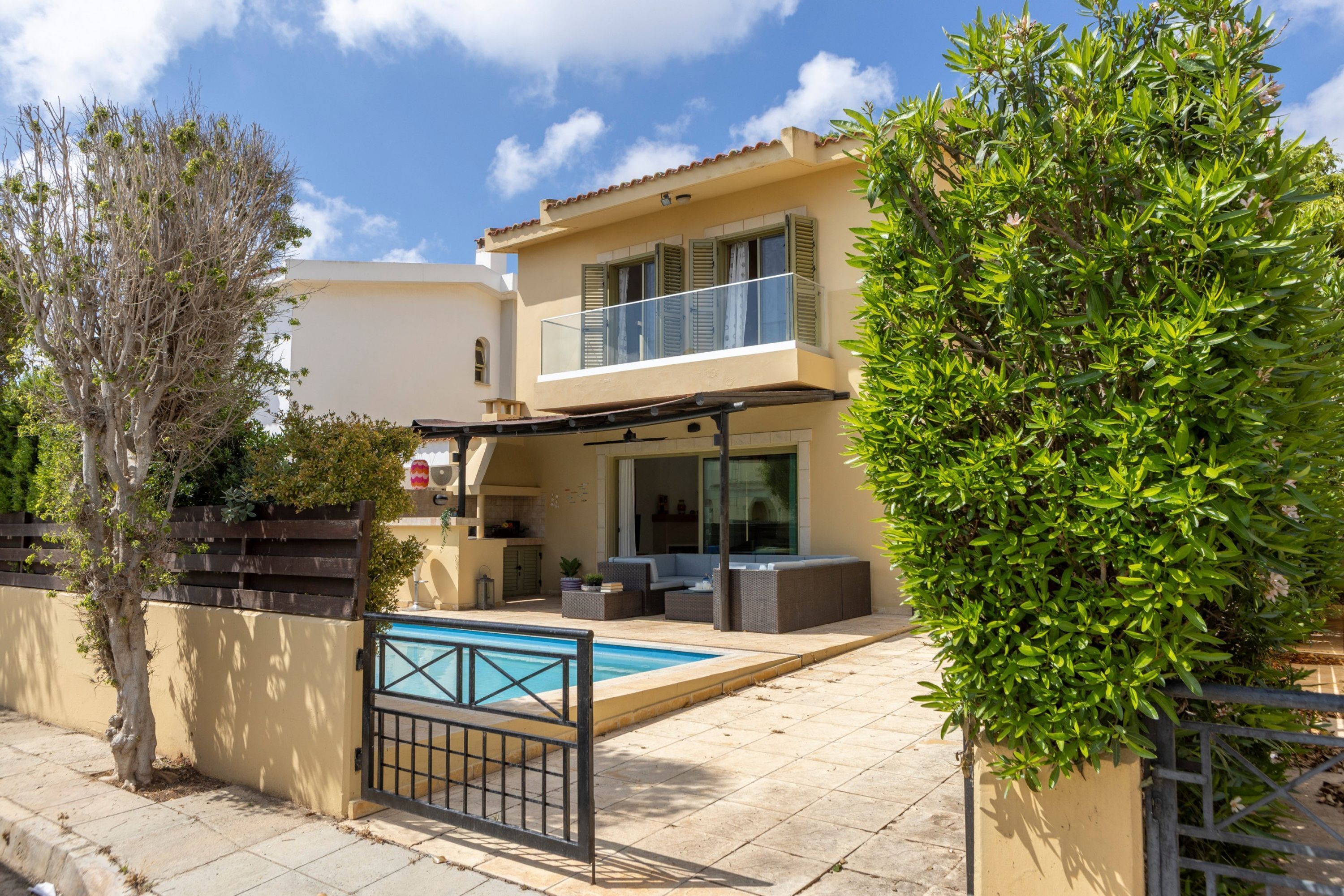 Uma casa de dois andares com piscina, área de estar ao ar livre e portão fechado.