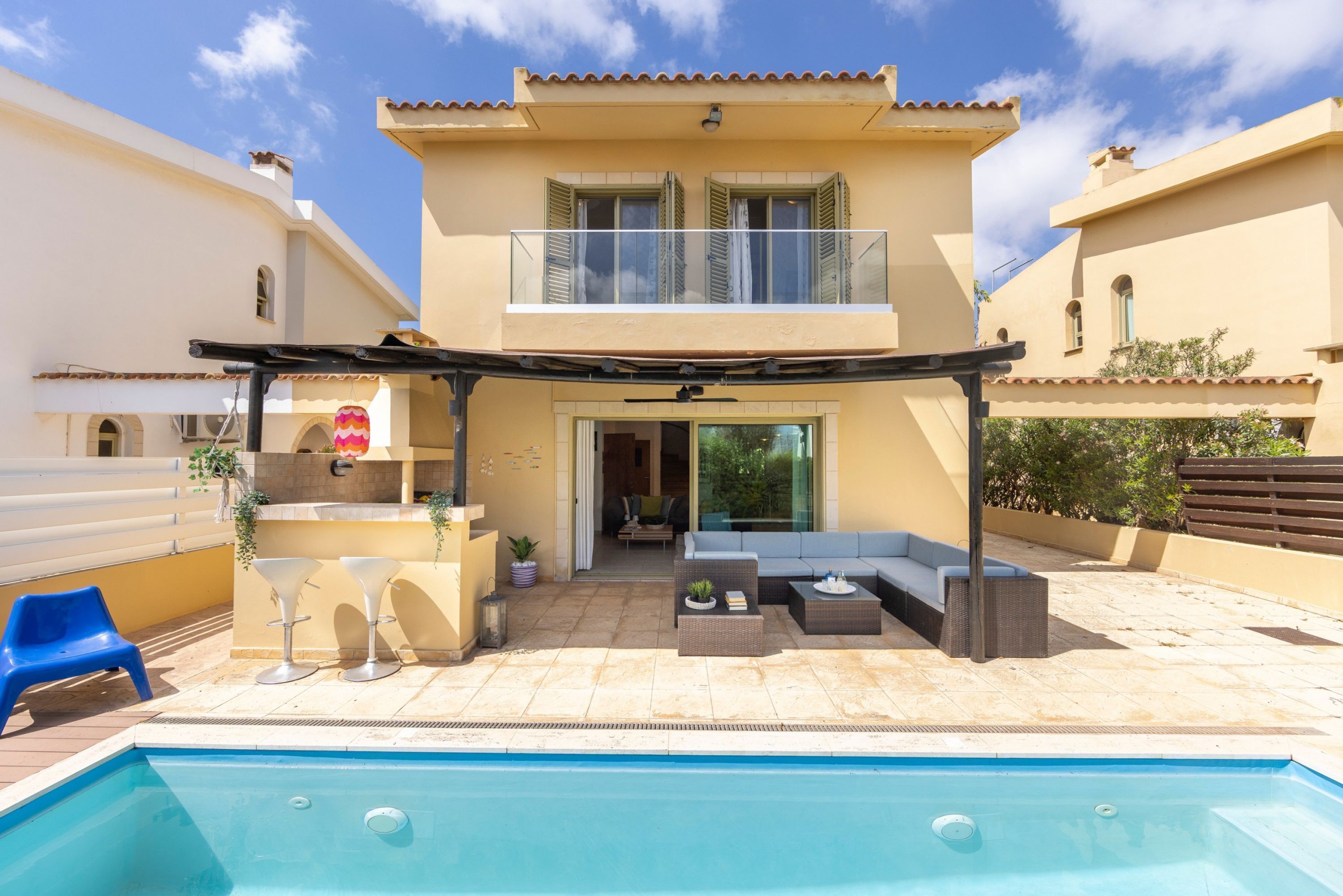 Uma casa de dois andares com varanda, piscina, área de estar ao ar livre e um pátio coberto.