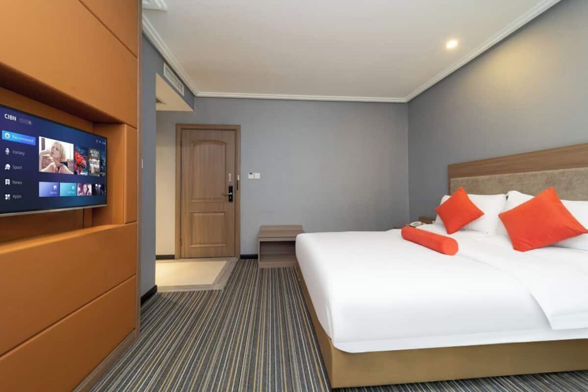 Quarto de hotel com uma cama, televisão na parede e porta de madeira.