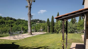 Uma área de pátio com móveis de exterior, uma pérgula e vista para uma paisagem verdejante.