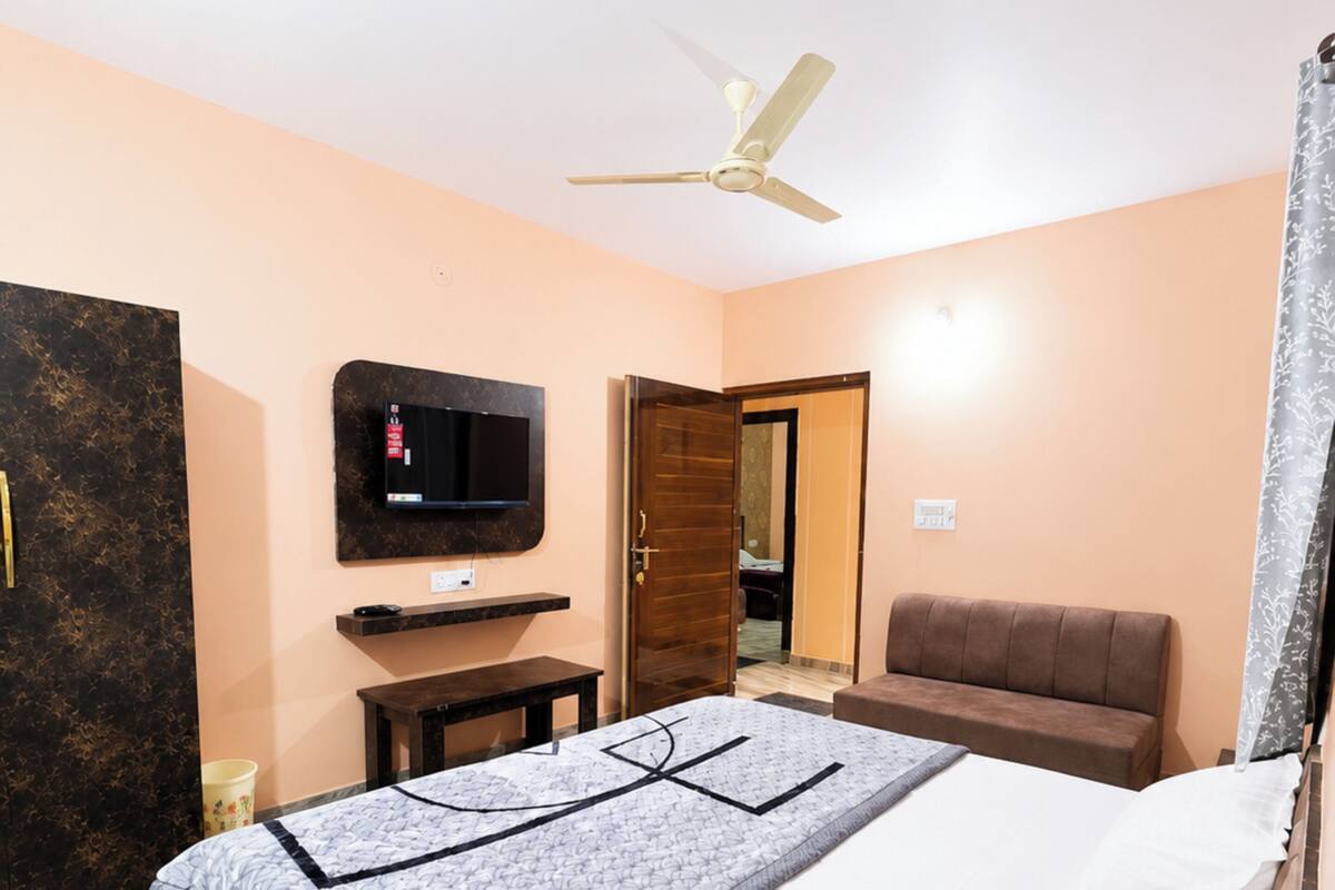 Quarto de hotel com cama, televisão, ventilador de teto, sofá e porta que dá para outro aposento.