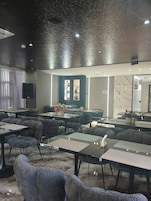 Sala de conferência com mesas e cadeiras, parede de mármore e teto com acabamento texturizado.
