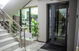 Uma entrada de hotel moderna com porta de vidro, escada com guarda-corpos de metal e plantas em vasos.