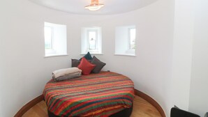 Quarto circular com cama, três janelas e uma luminária no teto.