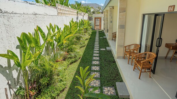 Corredor de hotel com caminho de azulejos, área de estar interna e parede branca com plantas.