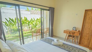 Quarto de hotel com uma cama grande, uma escrivaninha de madeira, uma cadeira e vista para um jardim através de uma porta de correr.