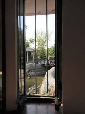Visão através de uma porta de vidro, com parede de pedra, uma pequena ponte e um lago.