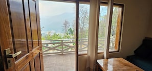 Um quarto com porta de madeira, janela com vista para uma varanda e uma mesa.