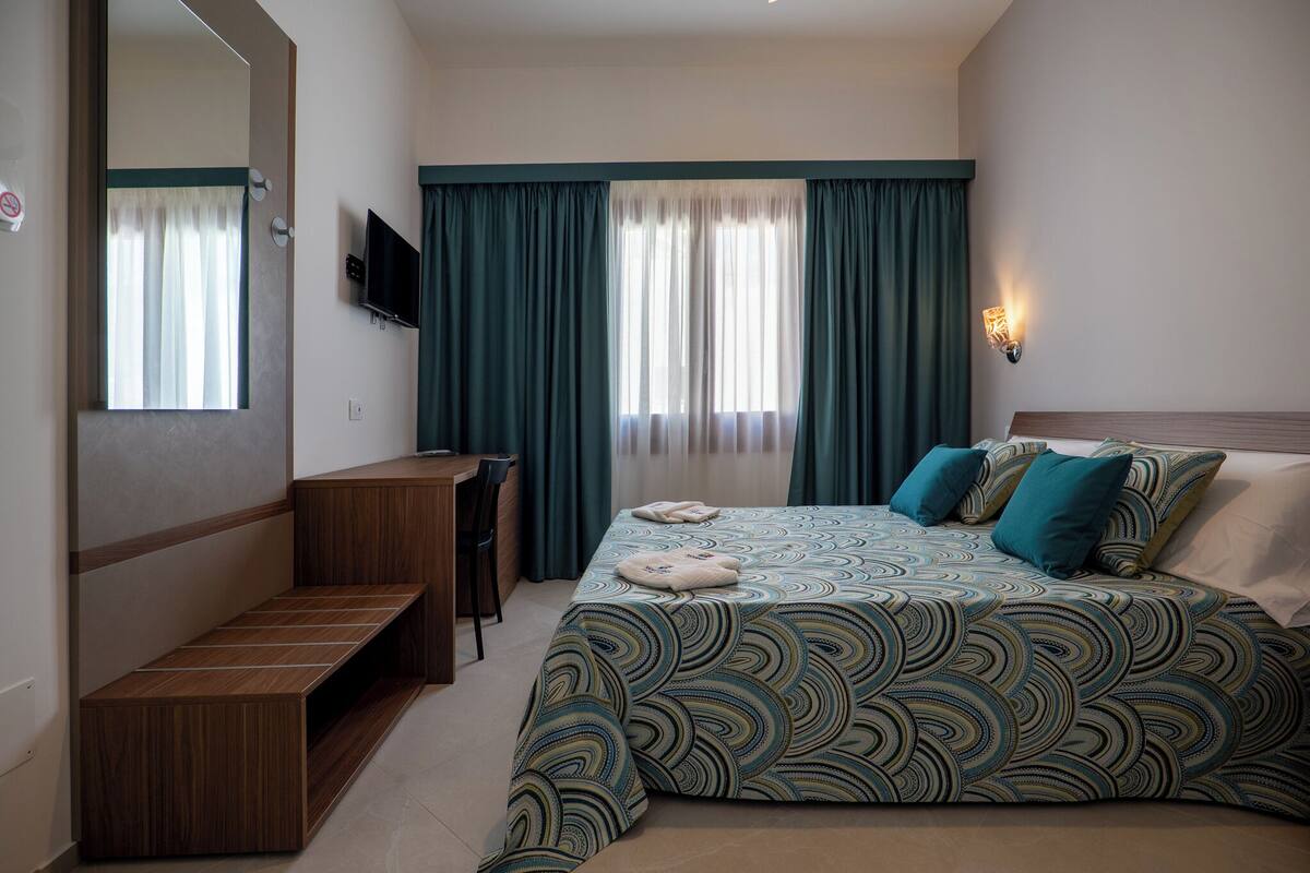 Quarto de hotel com cama, escrivaninha e televisão.